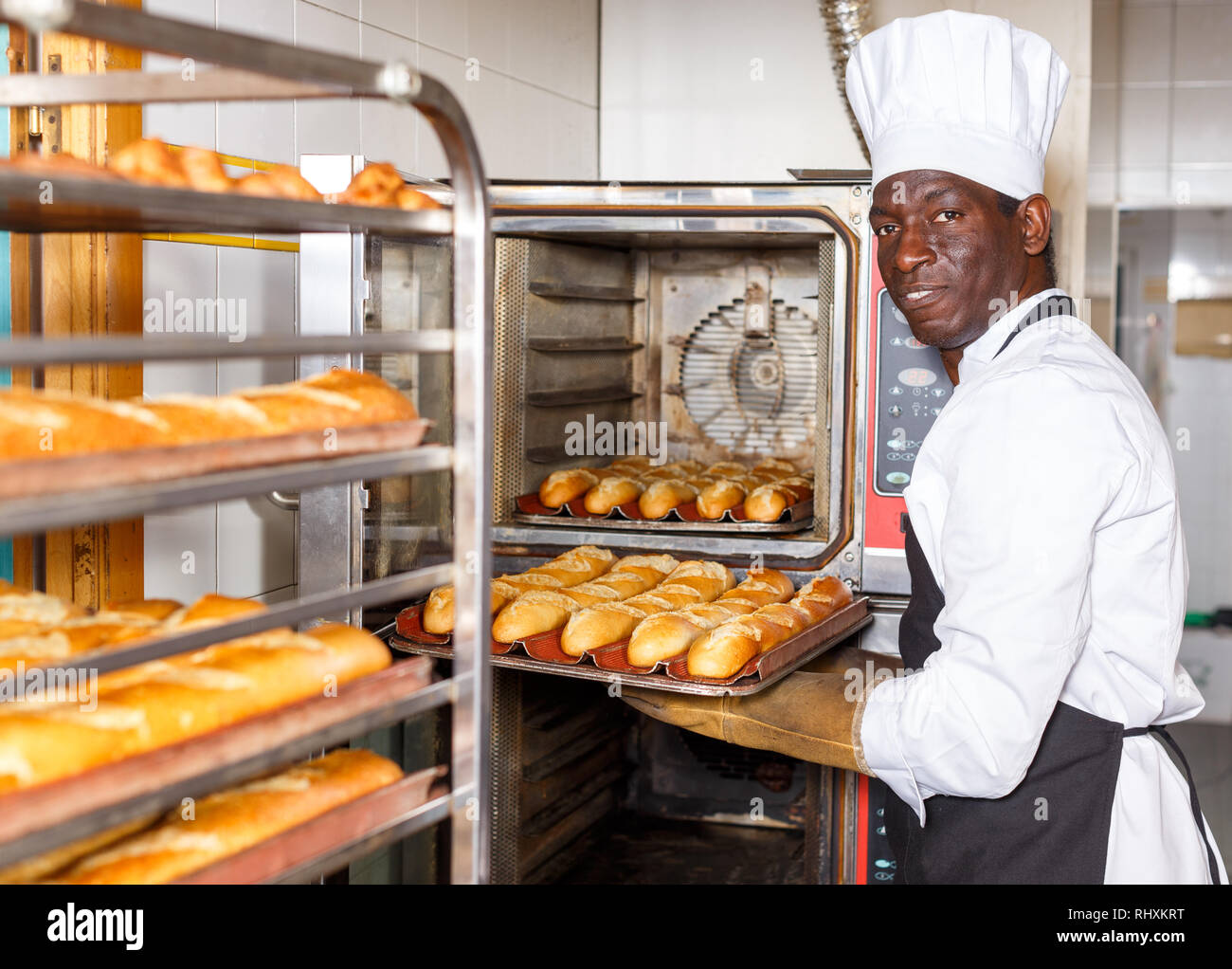 Portrait of African American baker putting fresh baked baguettes on ...