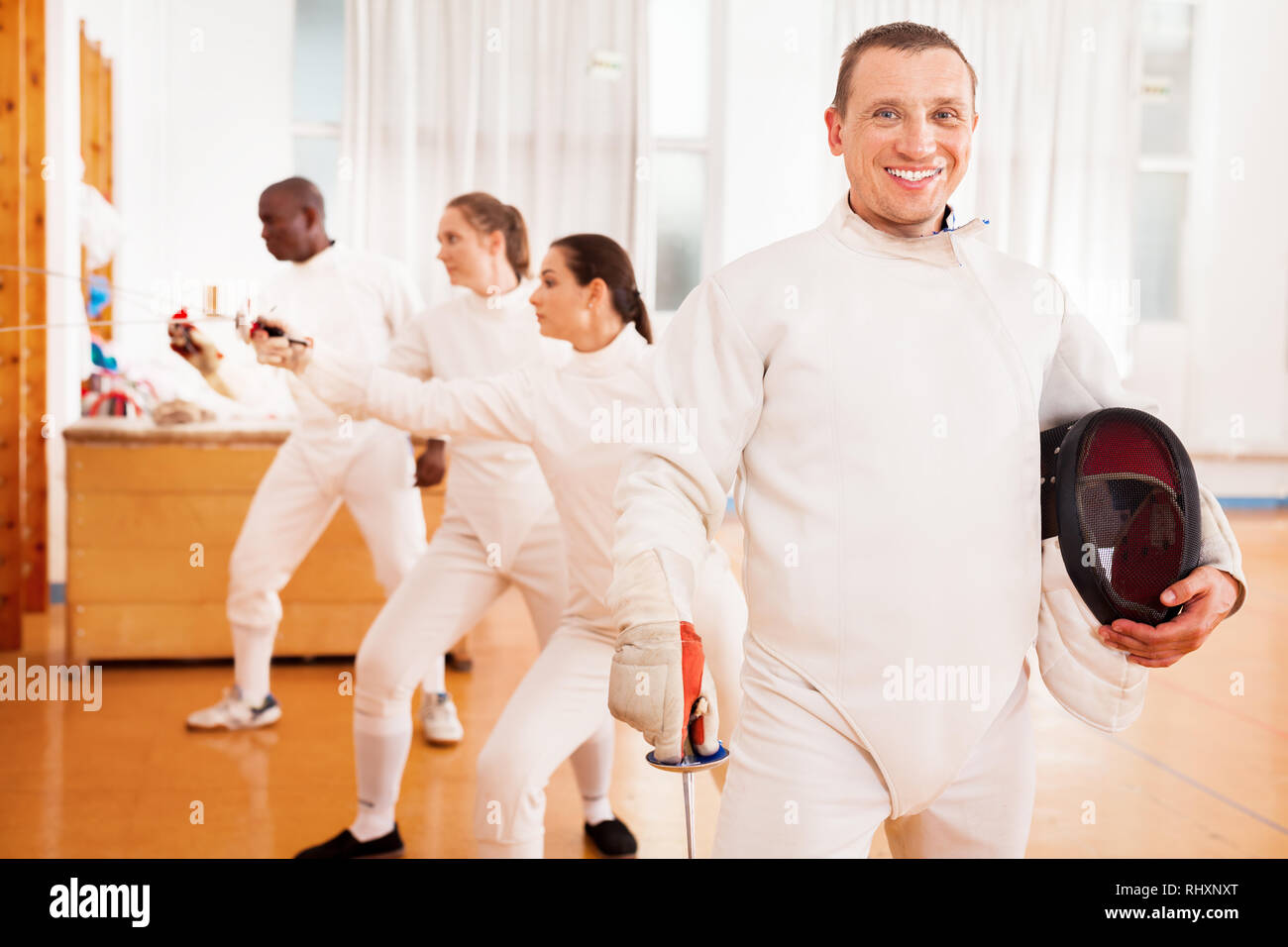 Sporty young man fencer in uniform standing with mask and a foil at ...