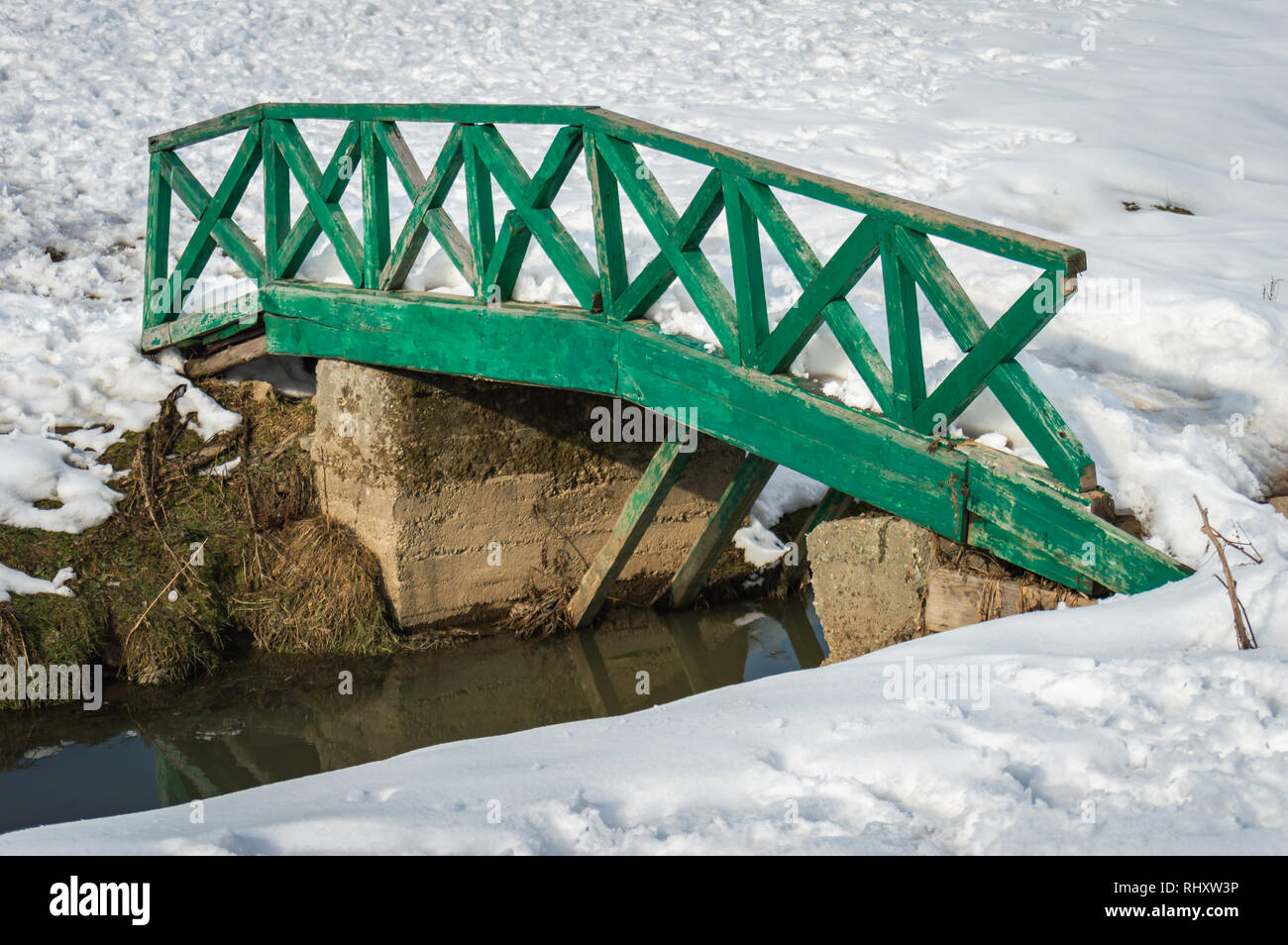 A green colour small wooden bridge over an small stream supported by ...