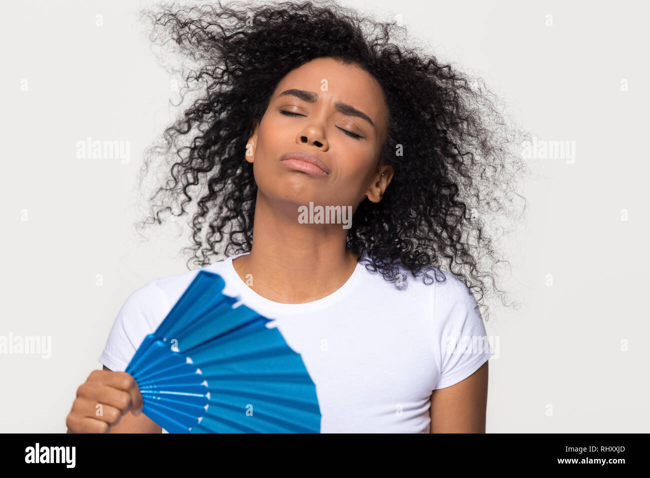 African woman sweating from heat waving fan isolated on background ...