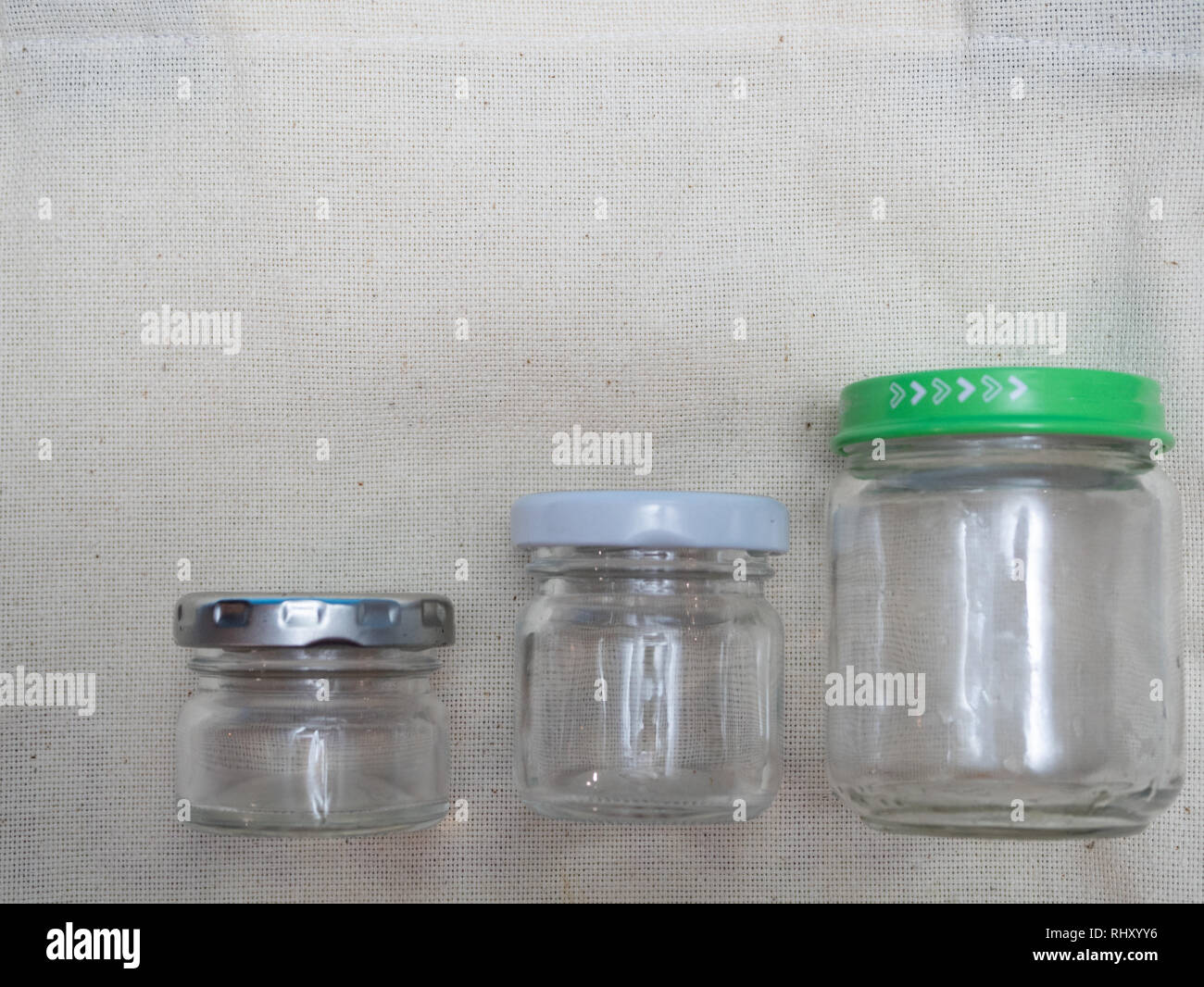 close-up of three small empty glass jars different sizes on fabric ...