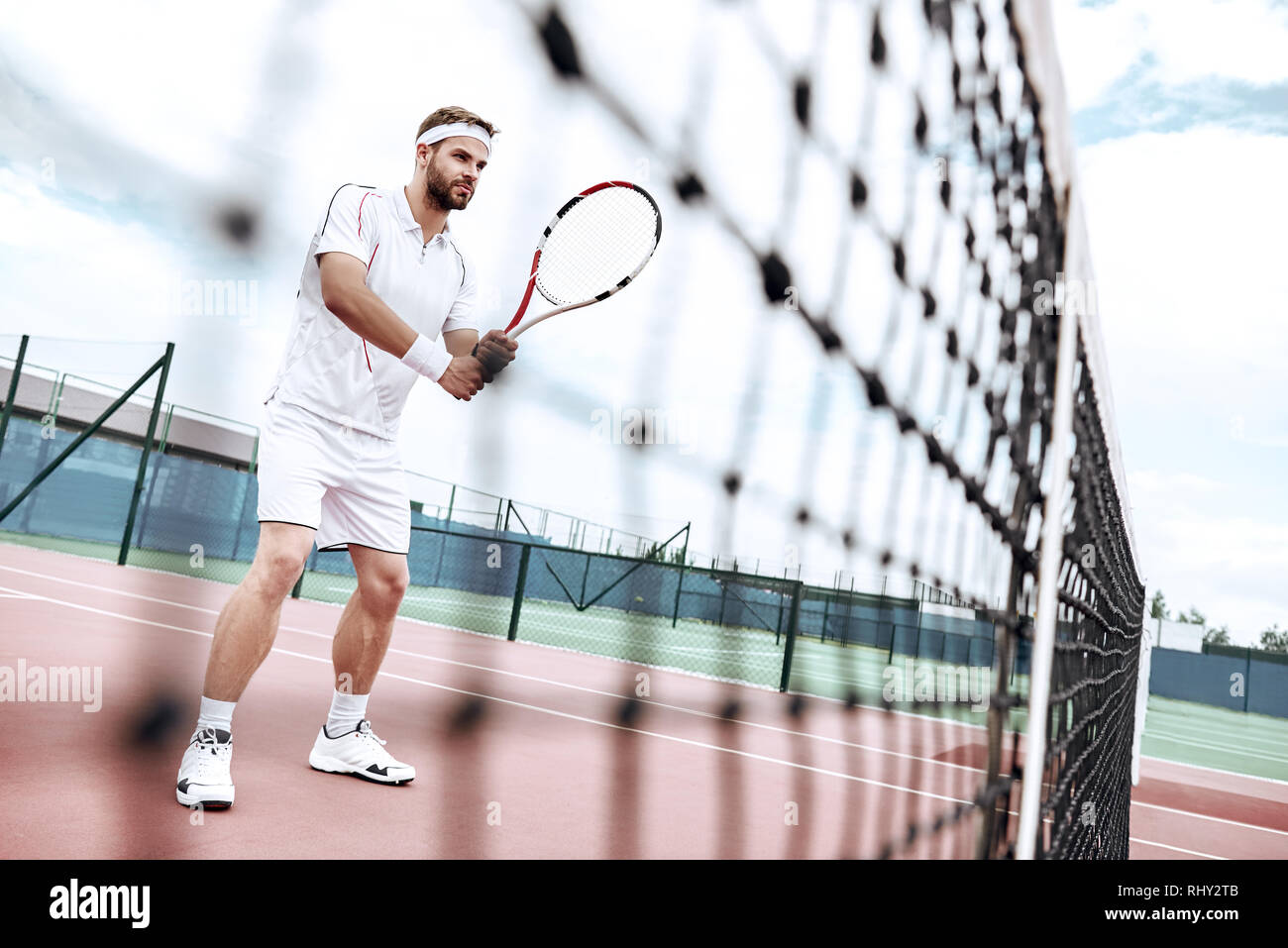 Handsome man holding tennis racket and looking concentrated while ...