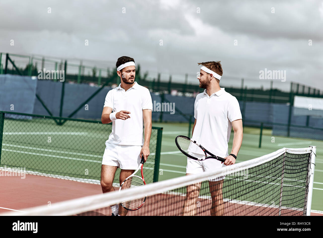 Handsome tennis players in white sportswear are discussing the upcoming ...