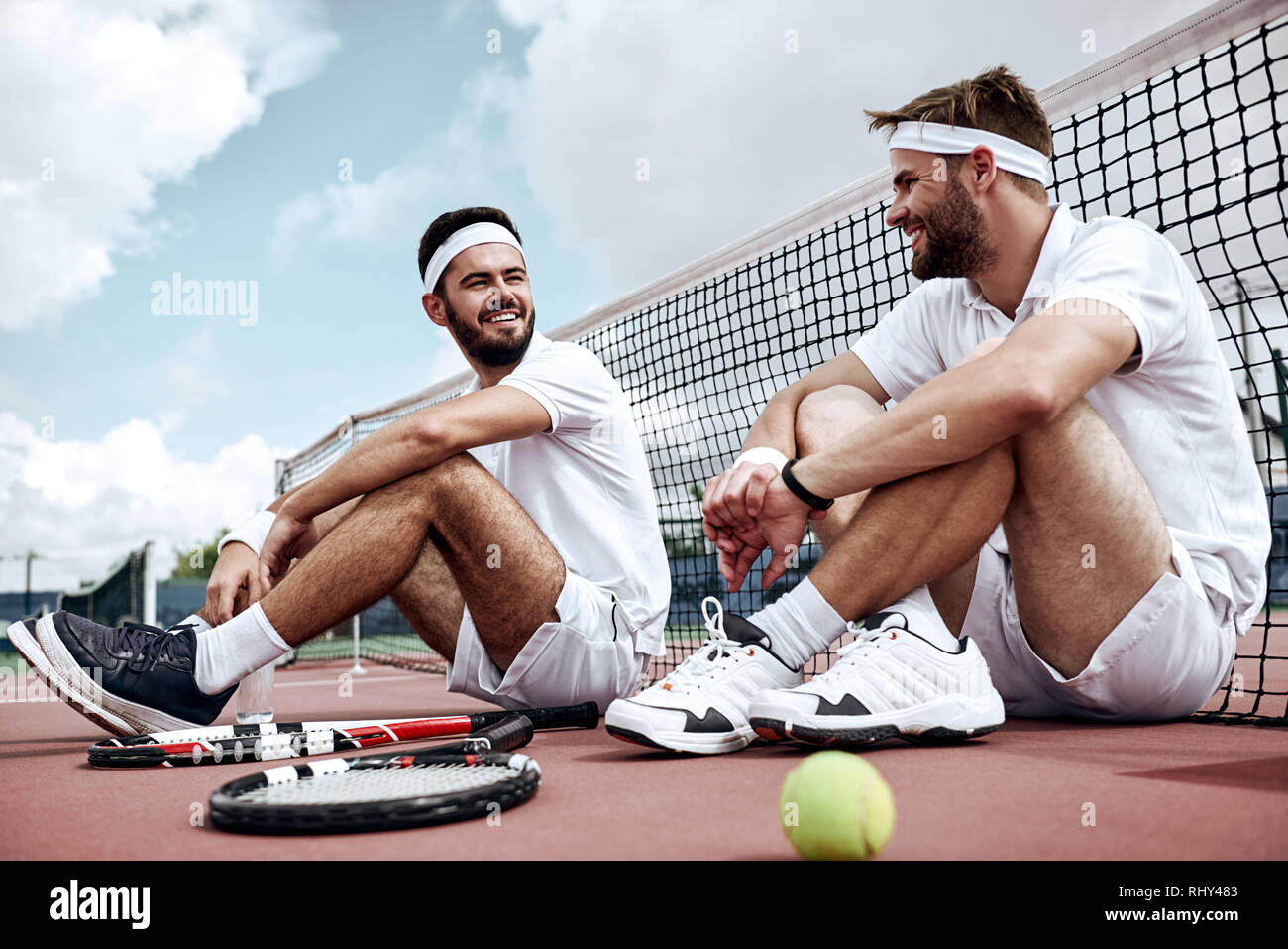 Two handsome tennis players are sitting on the court after the match ...