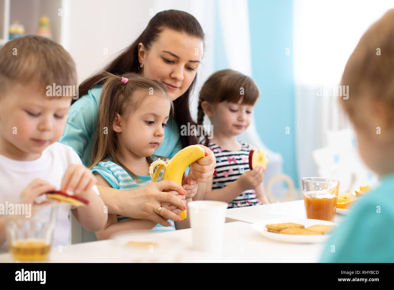 Kids have lunch. Children and carer together eat fruits in kindergarten ...