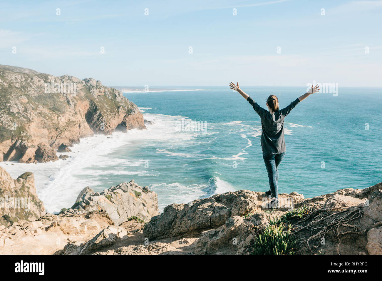 The girl next to the Atlantic Ocean in Portugal raises up her hands ...