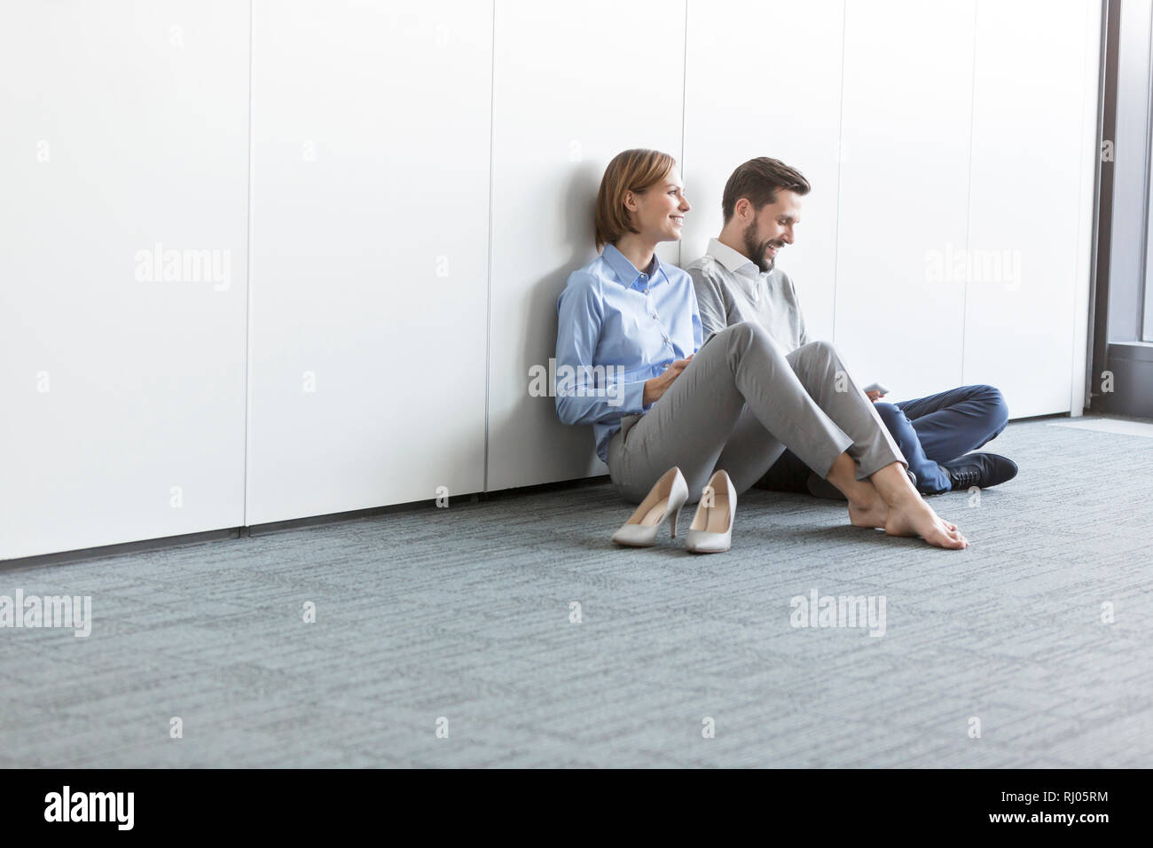 Smiling business people sitting against wall at office Stock Photo - Alamy