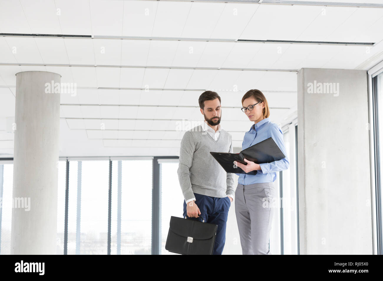 Business colleagues reading file while standing at new office Stock ...