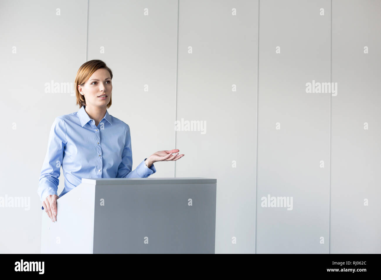 Confident businesswoman giving speech at podium against wall in office ...