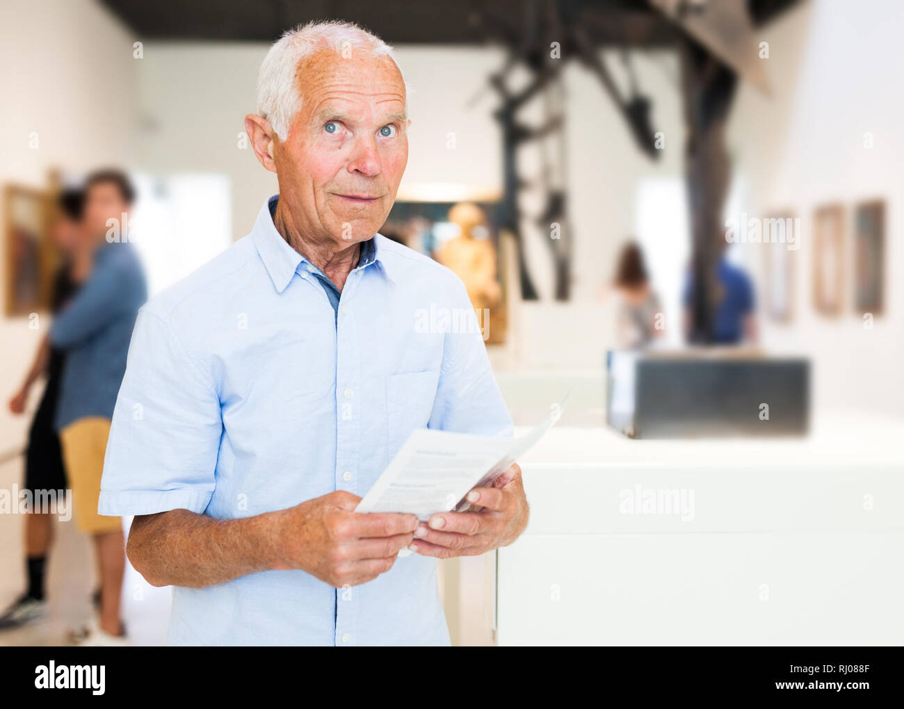 Positive mature man with guide in hands visiting historical museum ...