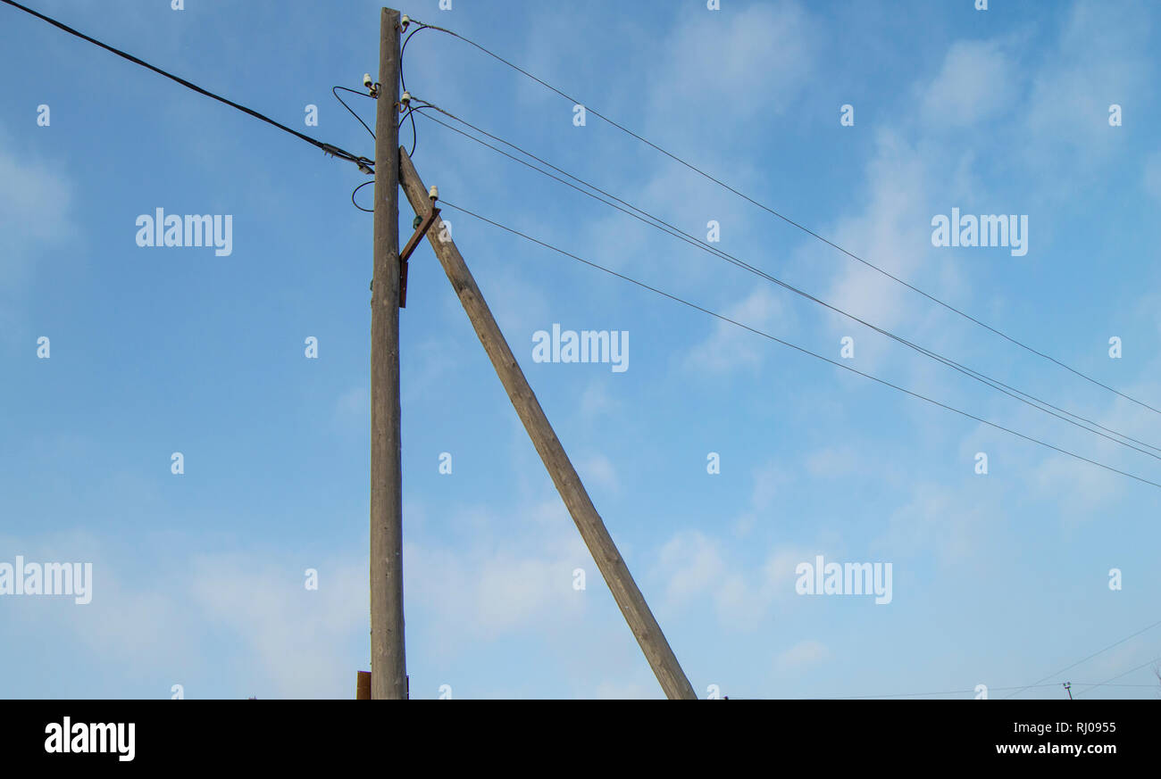 Wooden old 0.4 kV power line support with wires and insulators on blue ...