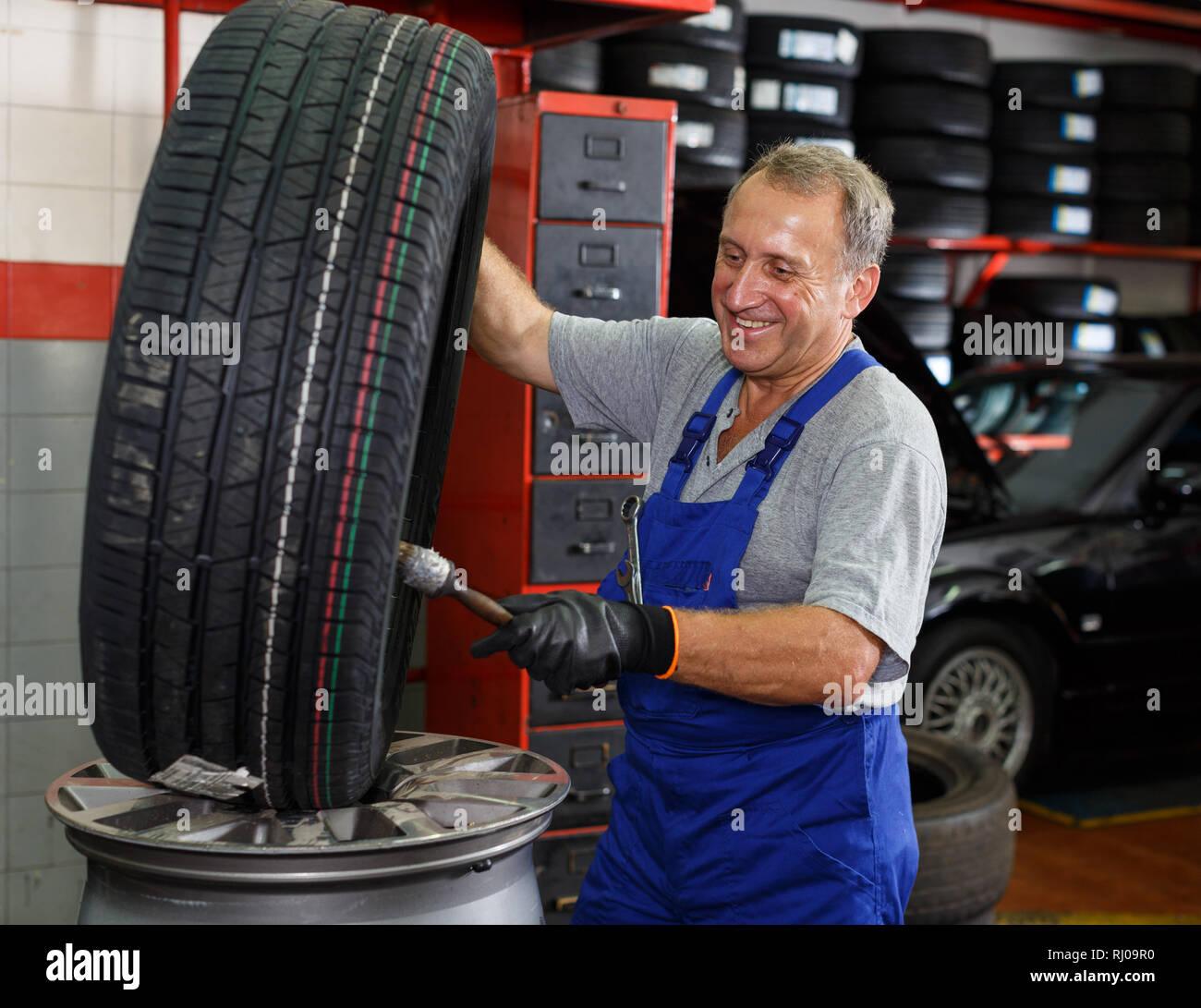 Elderly man mechanic engaged in repair of car wheel in auto workshop ...