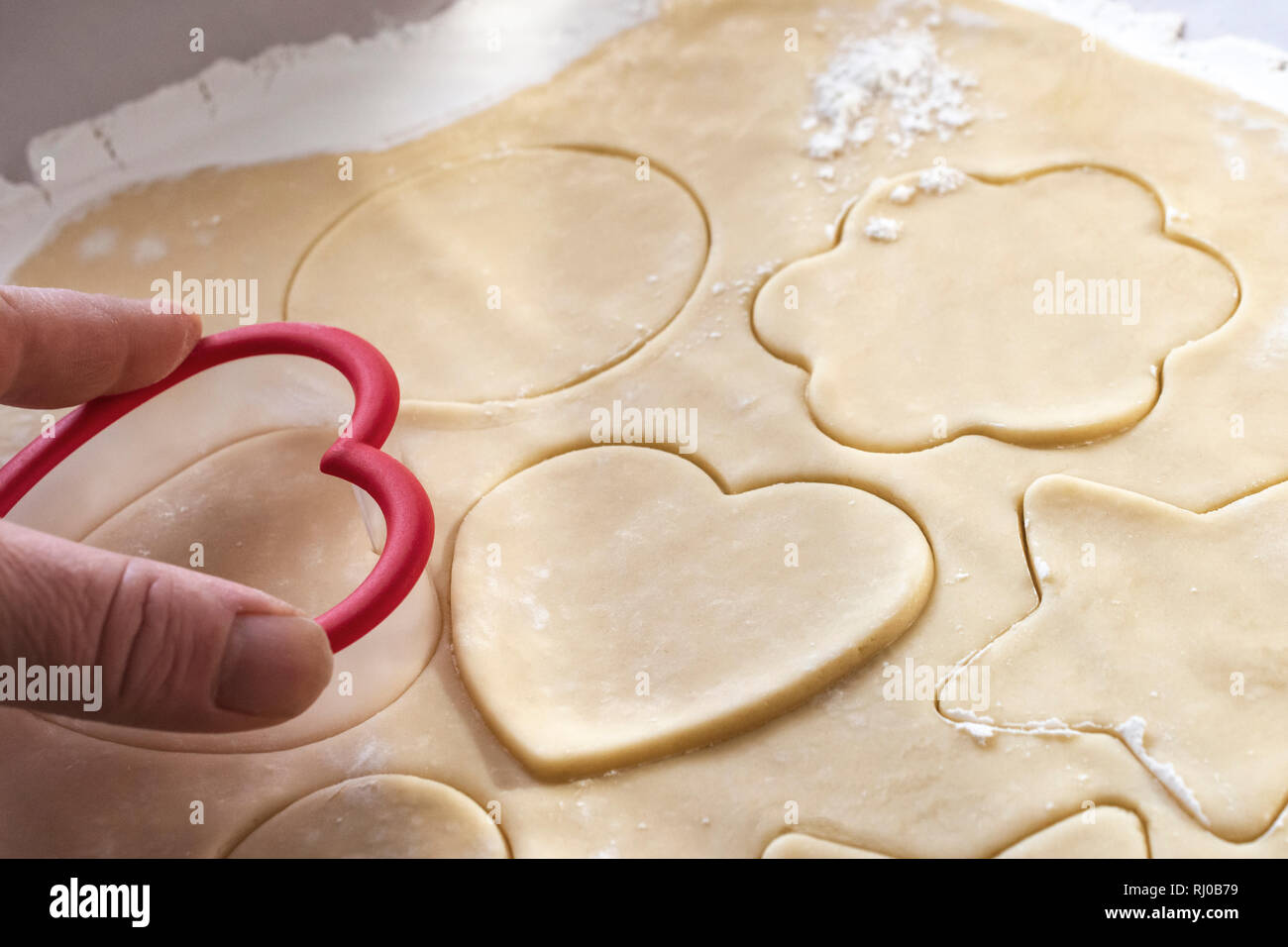 Fingertips pressing a heart shaped cookie cutter into a sheet of sugar ...