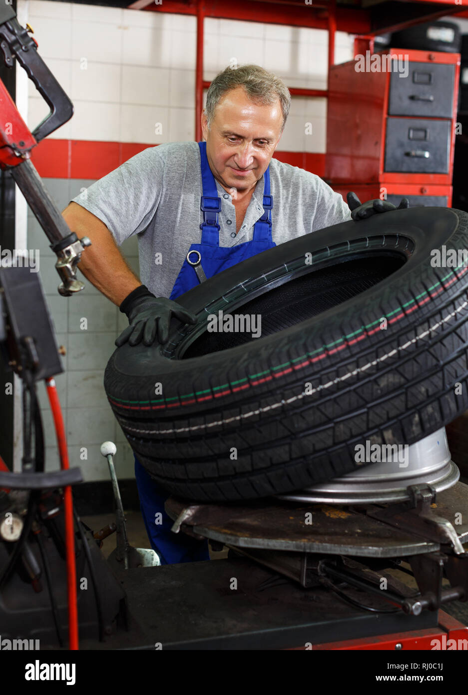 Mature man car mechanician removing tire from wheel disc in auto repair ...