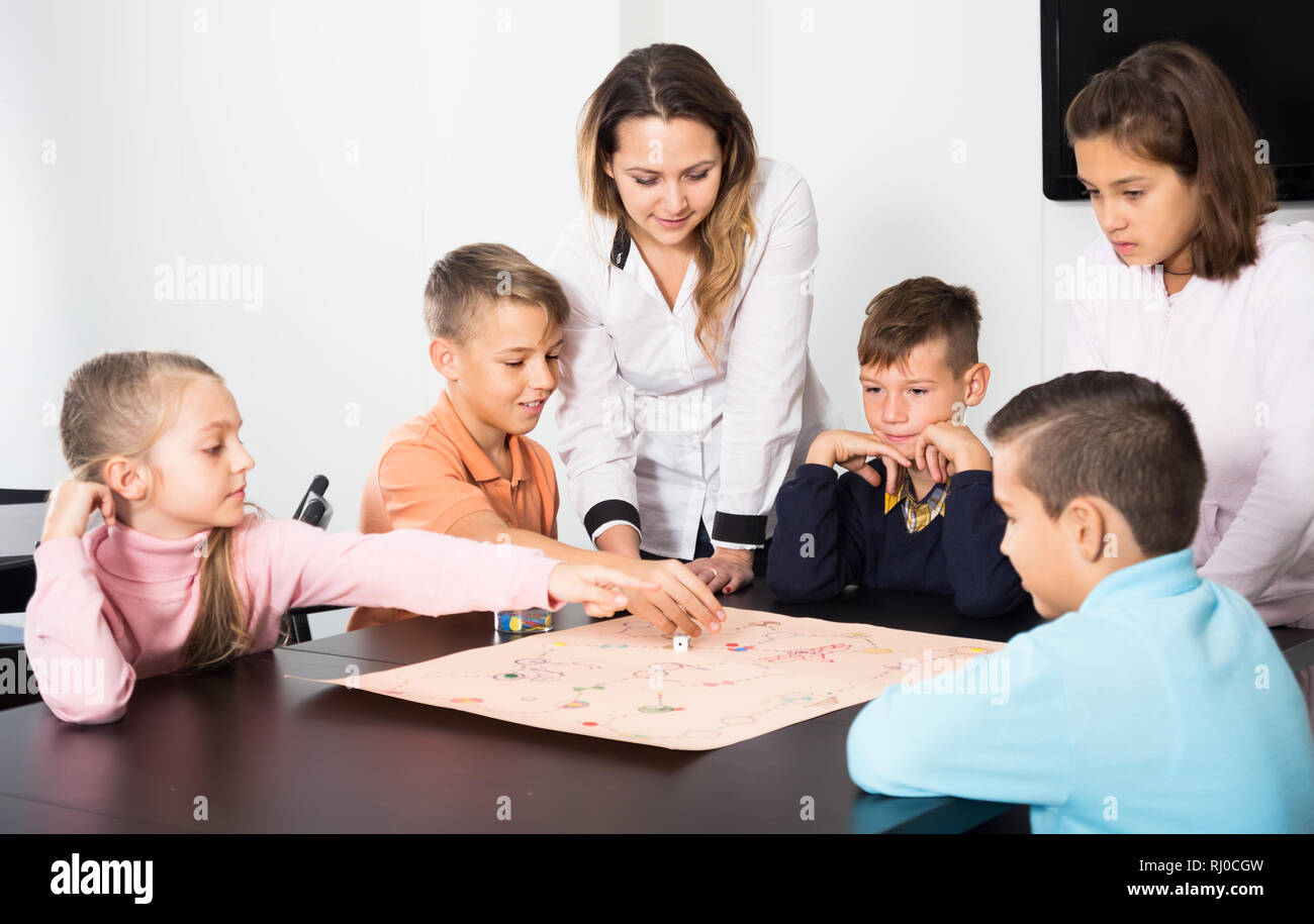 Elementary age happy kids sitting at table with board game and dice ...