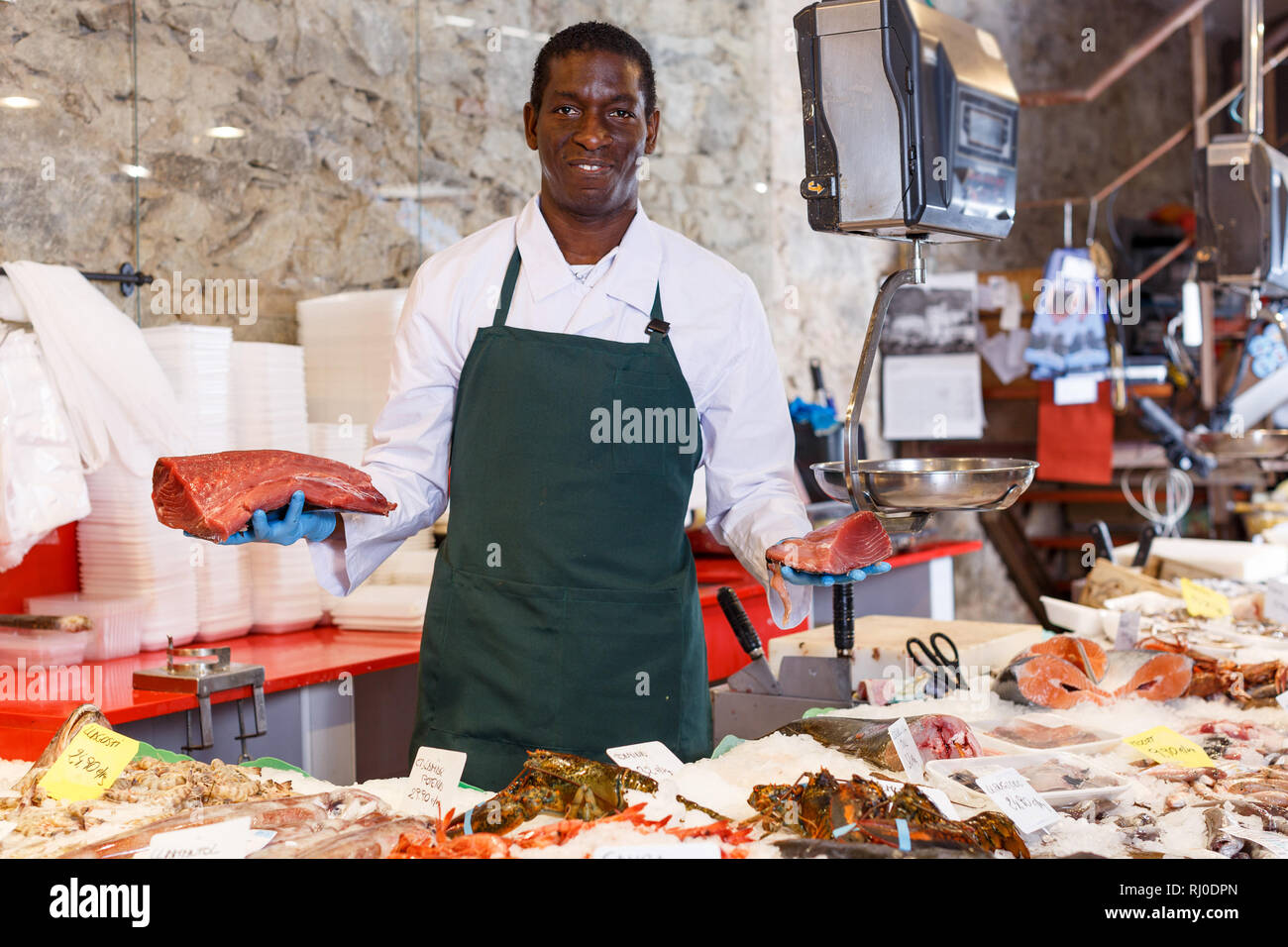 Portrait of African American salesman working at showcase with seafood ...