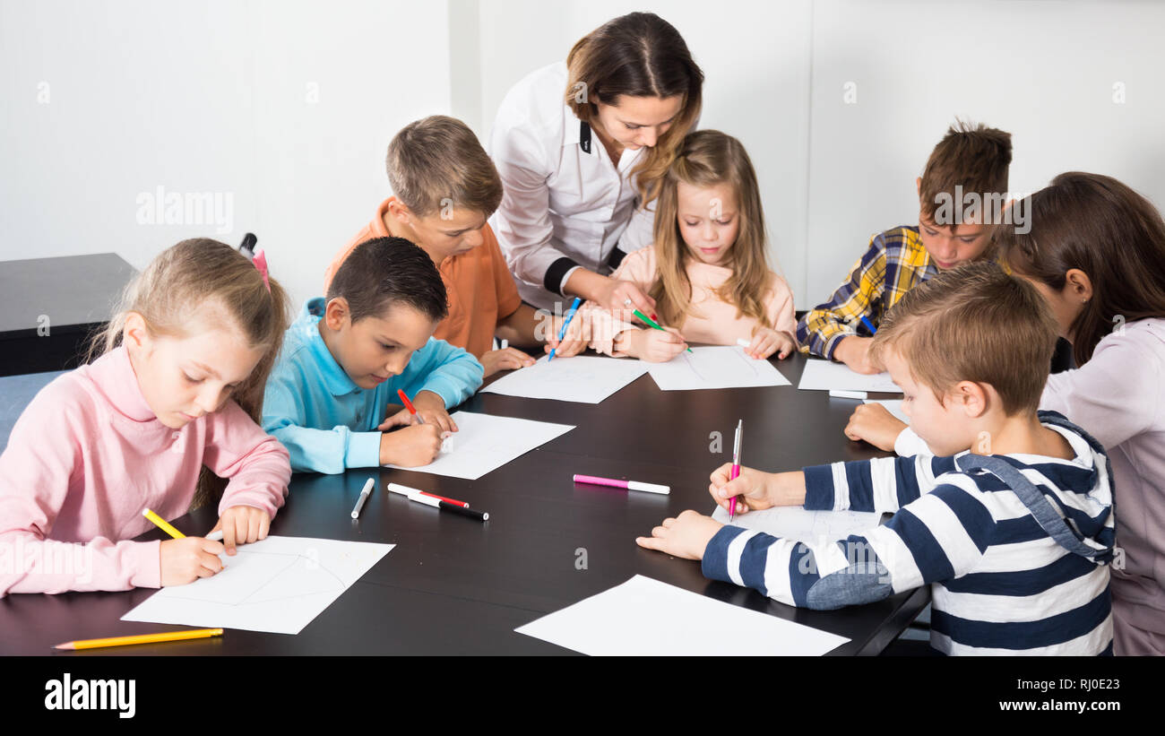 Teacher and elementary age children drawing at classroom in school ...