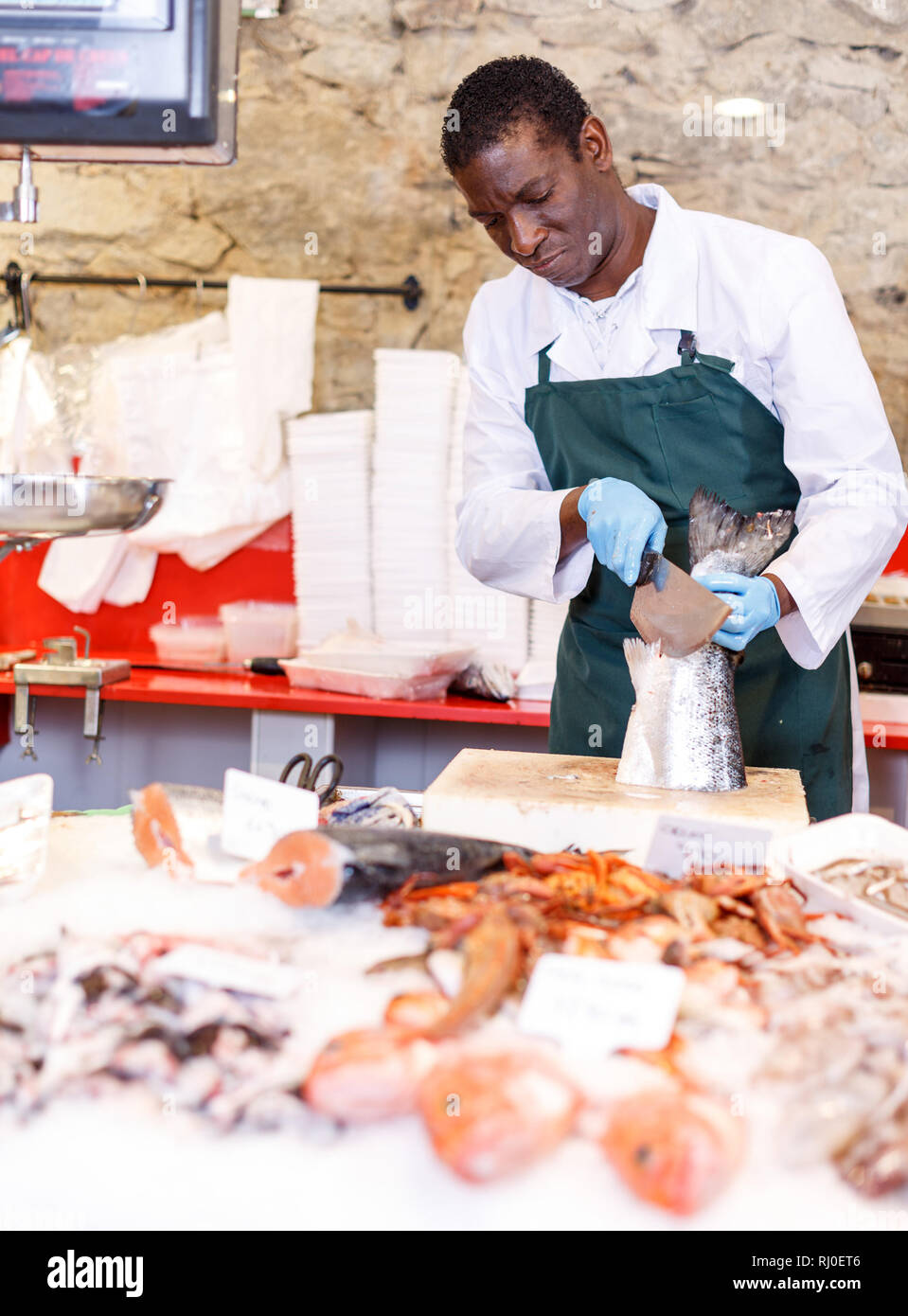African American seller preparing raw fish for customers at seafood ...