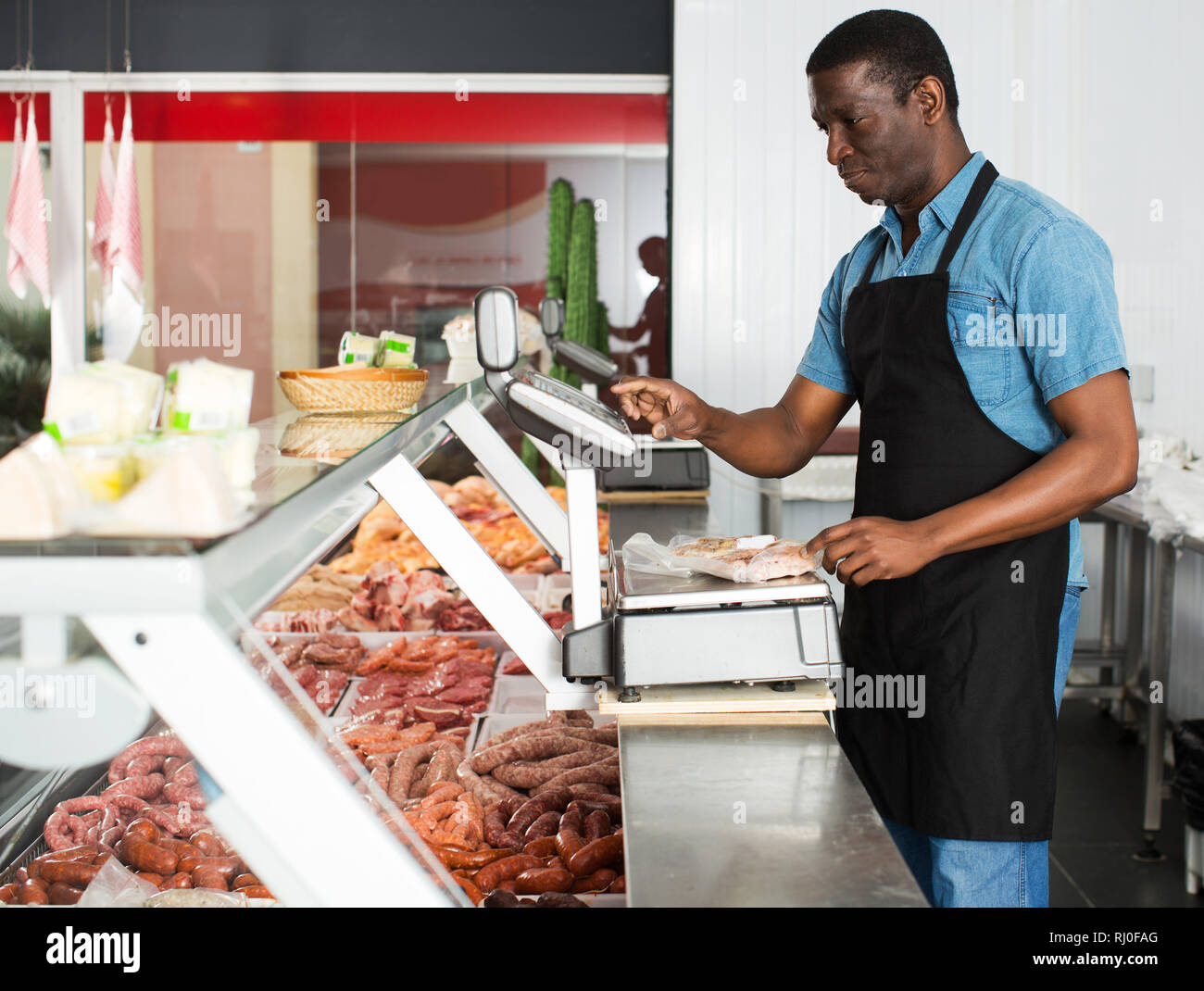 Professional positive butcher arranging meat products in display case ...