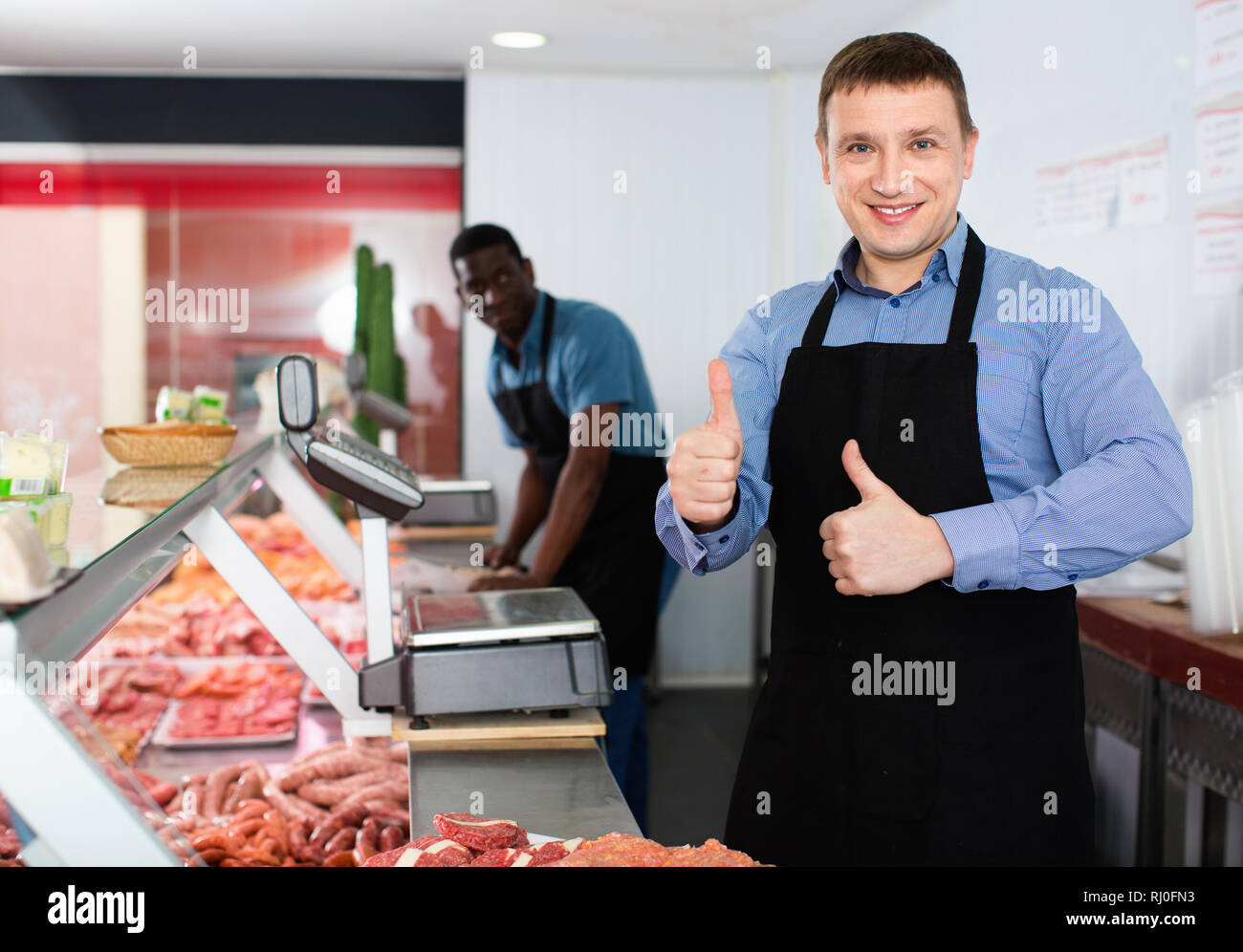 Proud cheerful smiling male owner of butcher shop standing behind ...