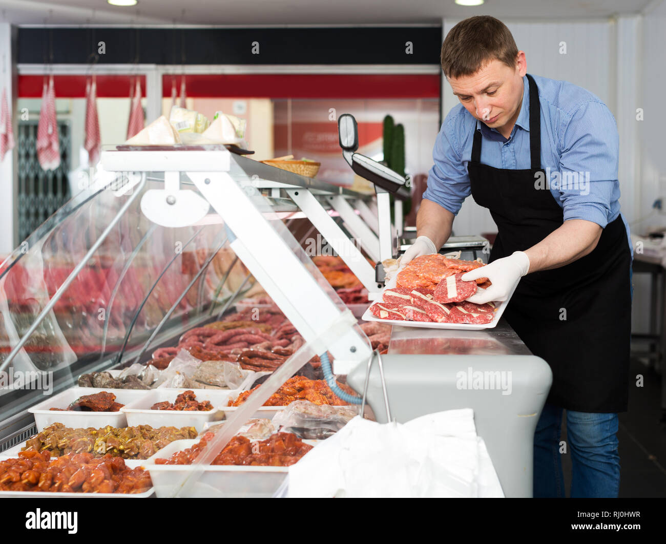 Professional adult butcher arranging meat products in display case of ...