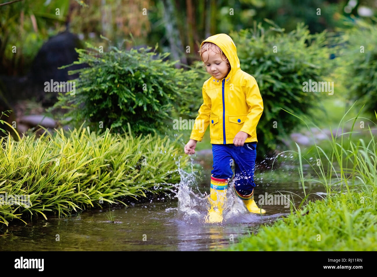 Kid playing in the rain in autumn park. Child jumping in muddy puddle ...
