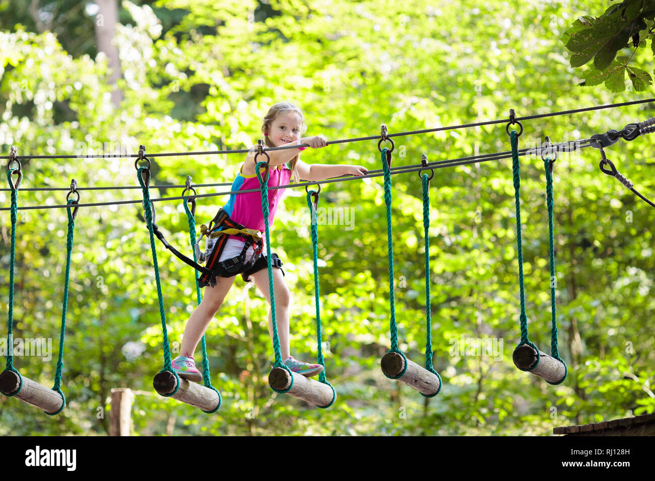 Child in forest adventure park. Kids climb on high rope trail. Agility ...