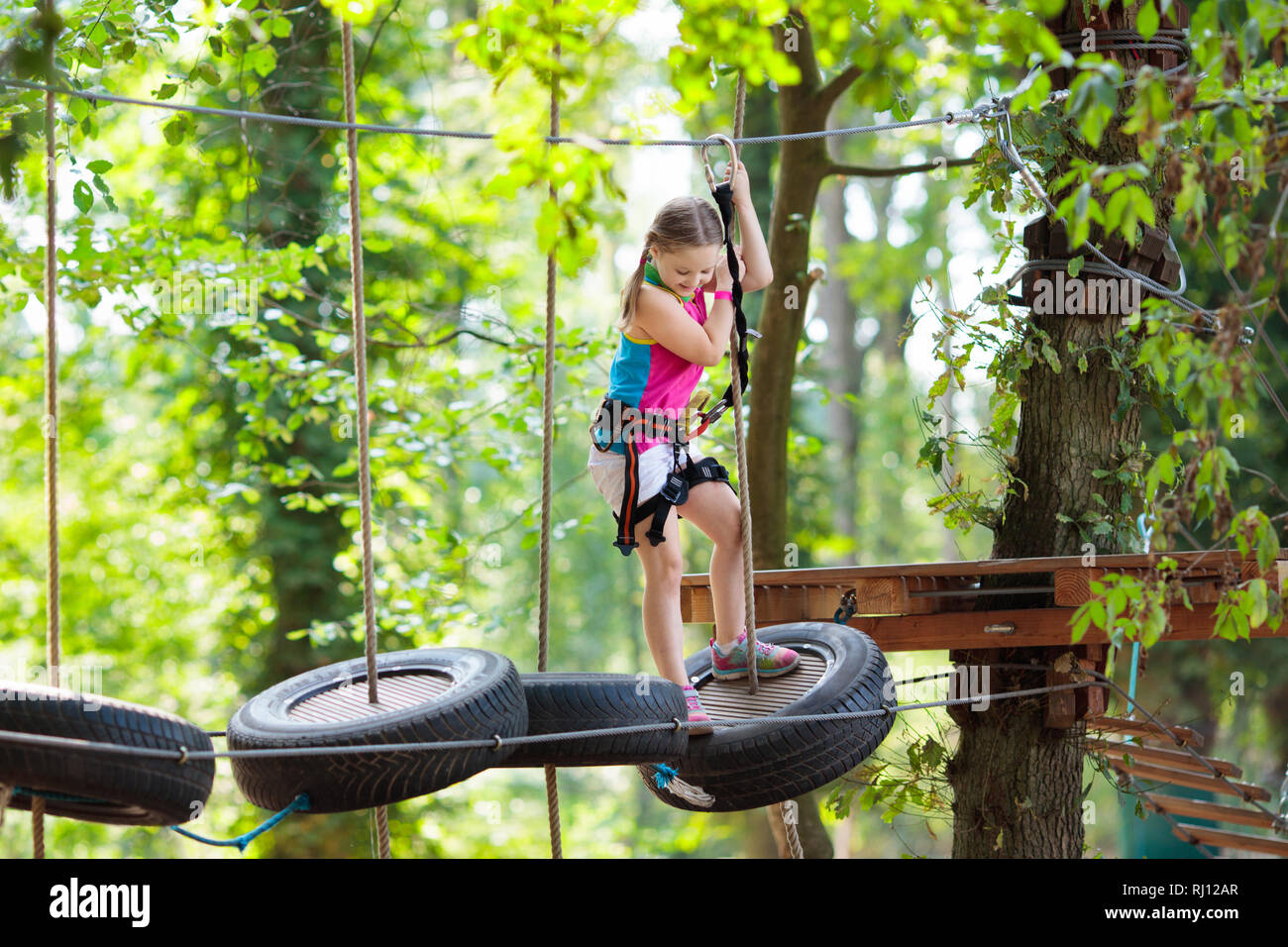 Child in forest adventure park. Kids climb on high rope trail. Agility ...