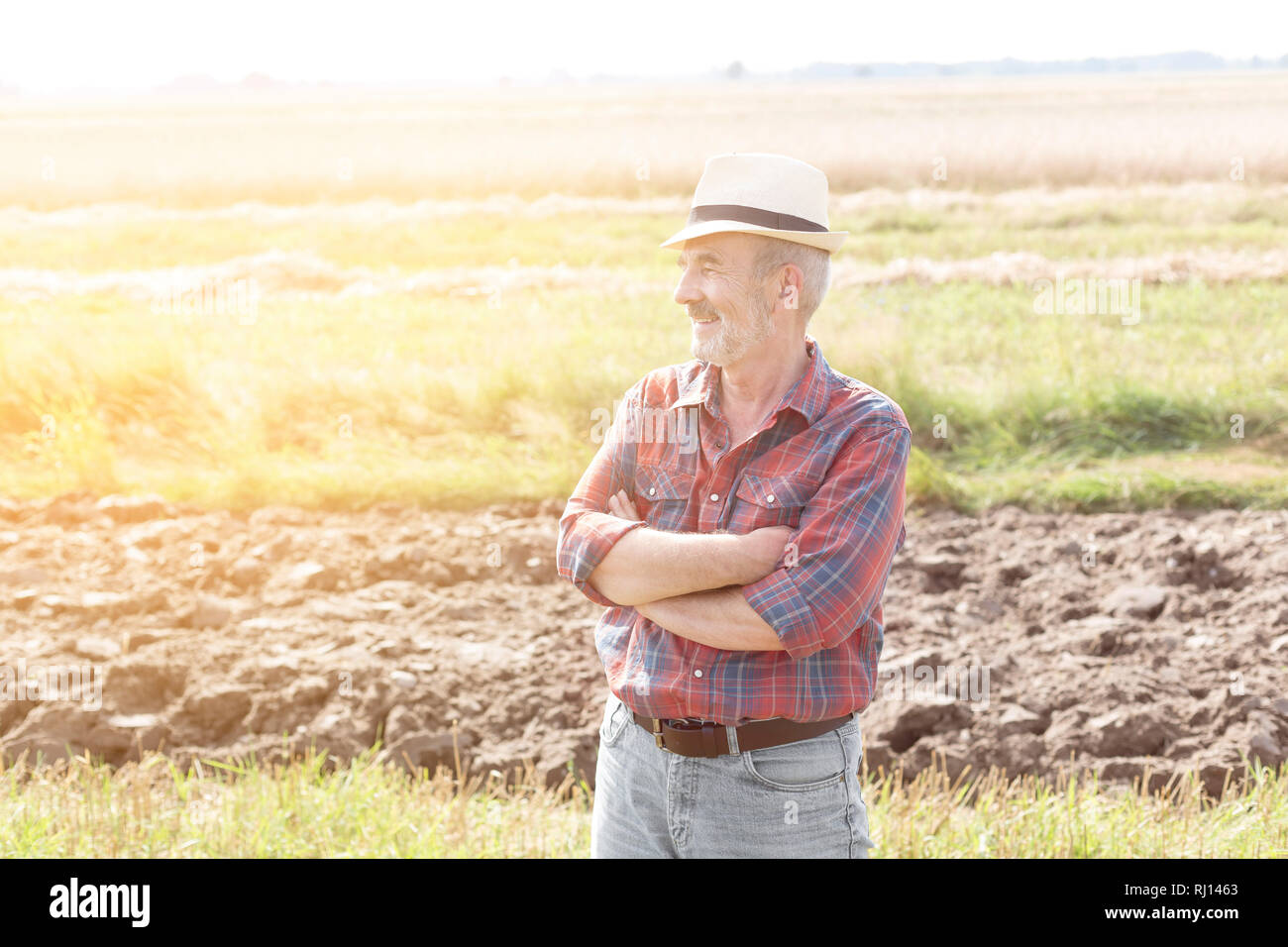 Smiling farmer standing with arms crossed on field at farm Stock Photo ...