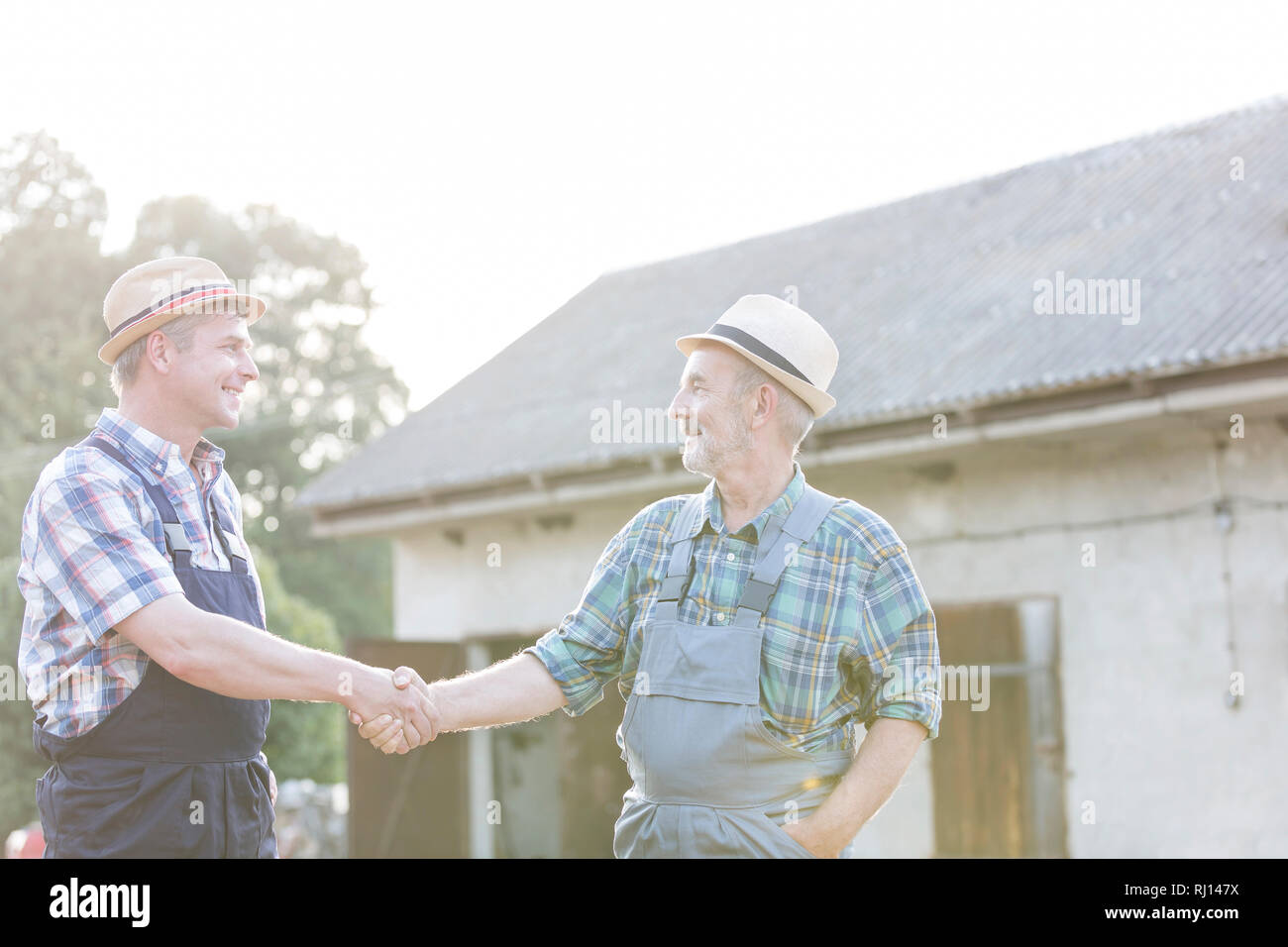 Farmers shaking hands while standing against barn at farm Stock Photo ...