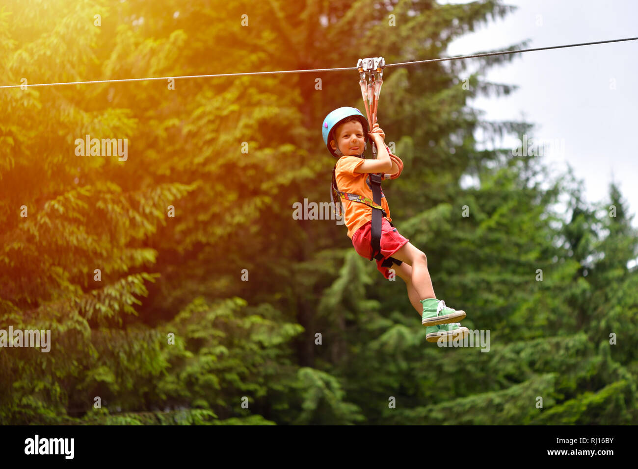 Happy kid with helmet and harness on zip line between trees Stock Photo ...
