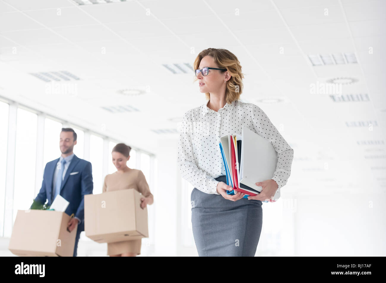 Businesswoman carrying files while colleagues talking with cardboard ...