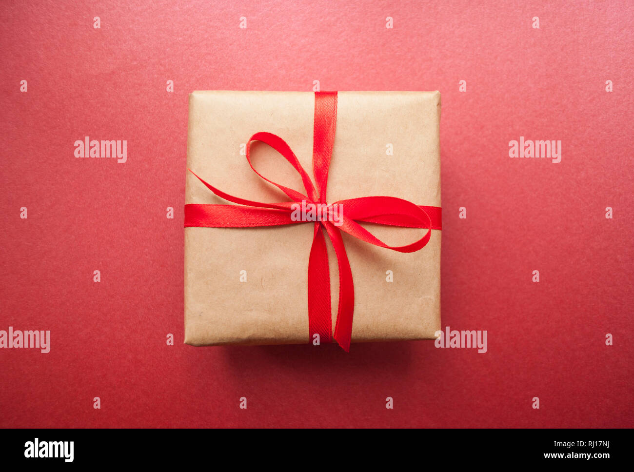Gift box wrapped in brown colored craft paper and tied with red bow on ...