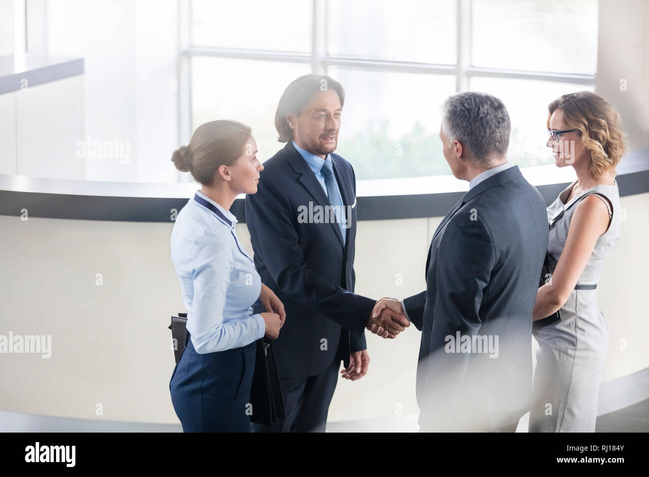 Businessmen greeting while standing with colleagues at reception in ...