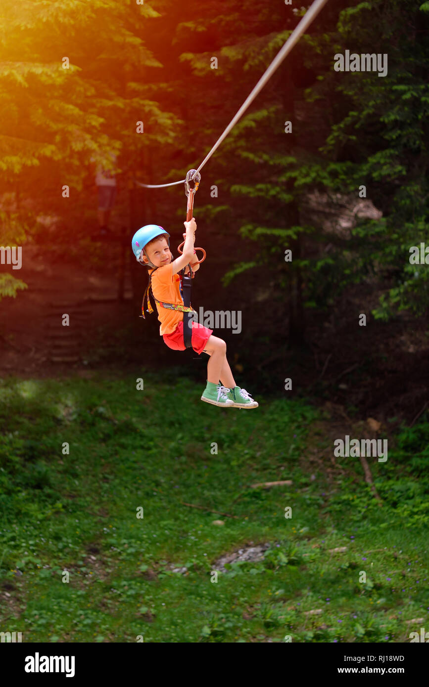 Happy kid with helmet and harness on zip line between trees Stock Photo ...