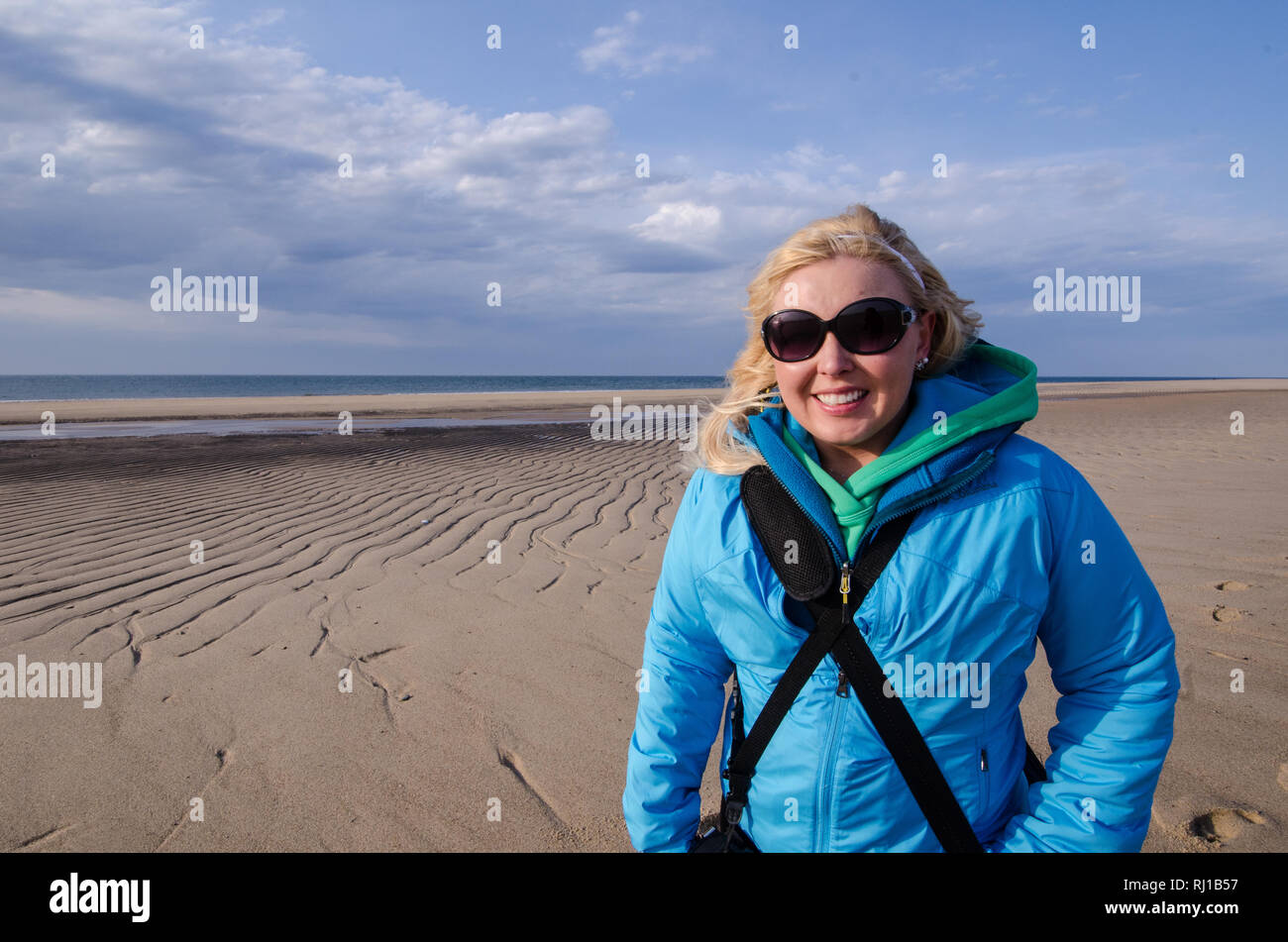 Woman wearing winter jacket and gear on the beach at Cape Cod National Seashore in early spring ...