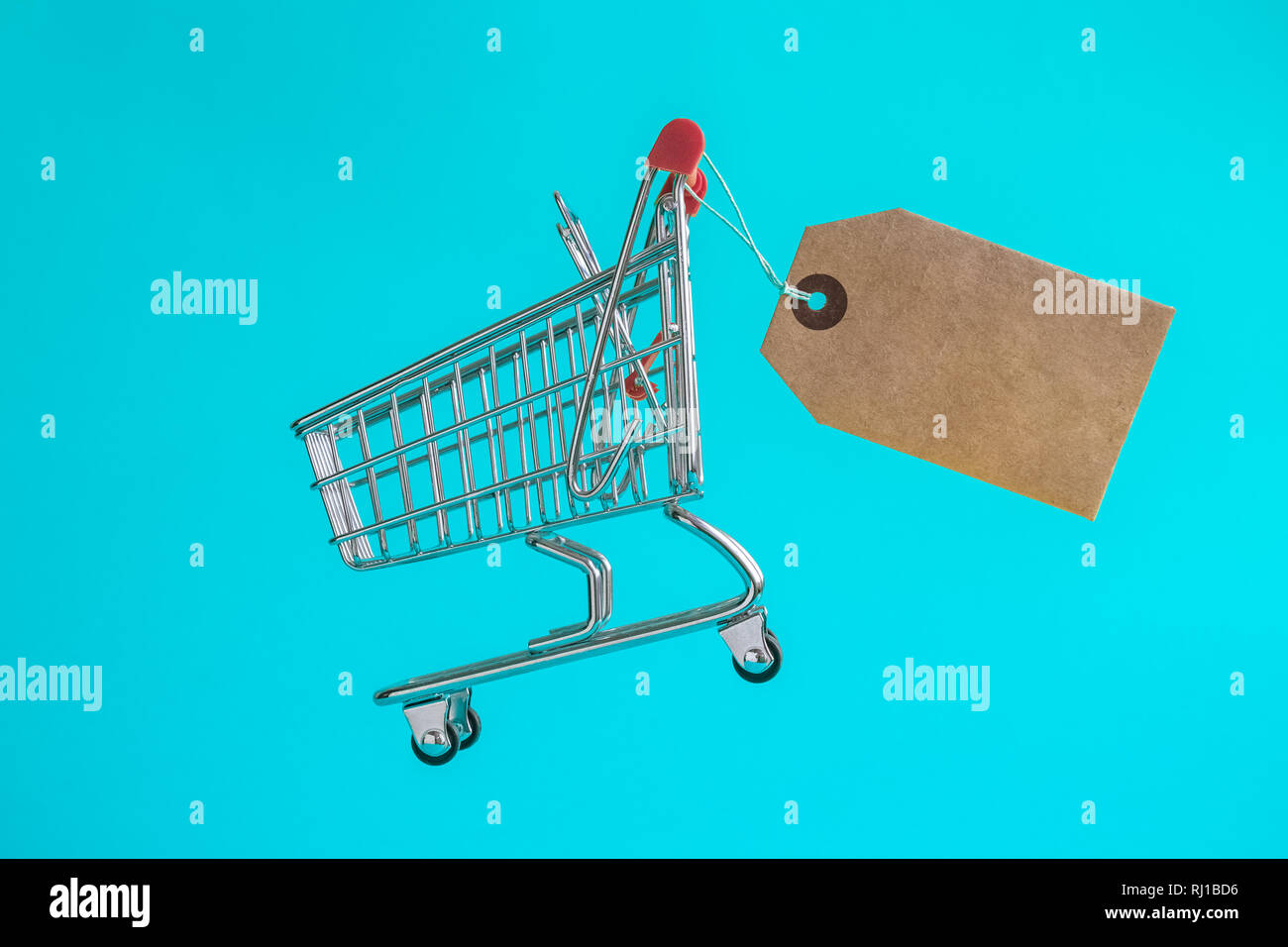 Small shopping cart with blank price tag on light blue background ...