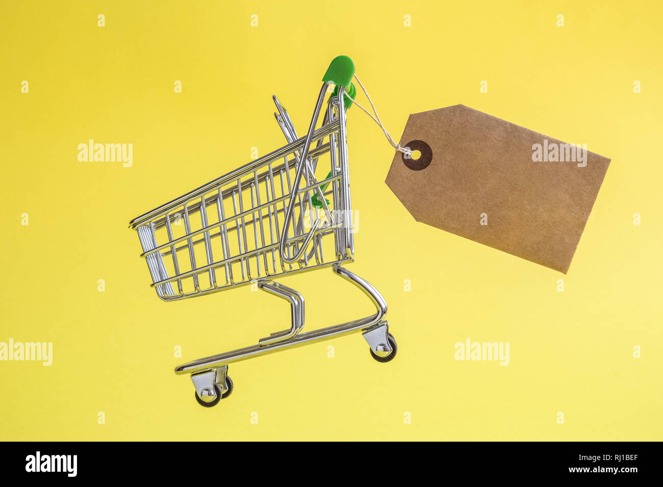 Small shopping cart with blank price tag on yellow background minimal ...