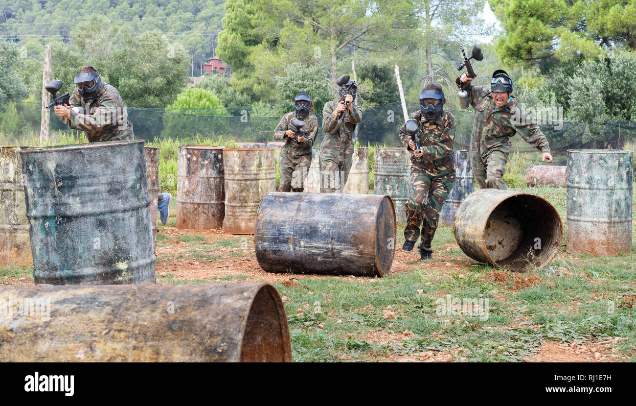 Team of cheerful smiling adult people playing paintball on battlefield ...