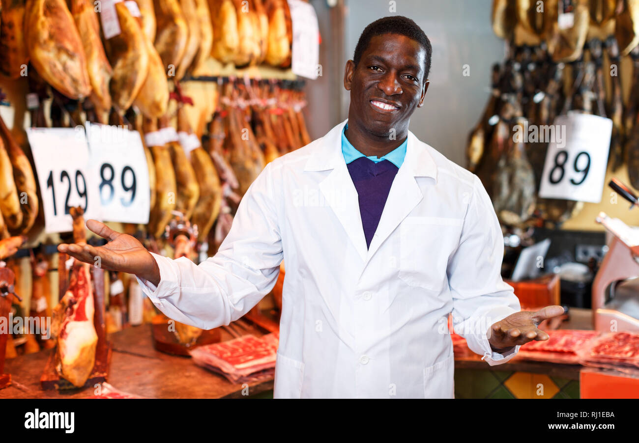 Happy African American seller working in meat shop, recommending ...