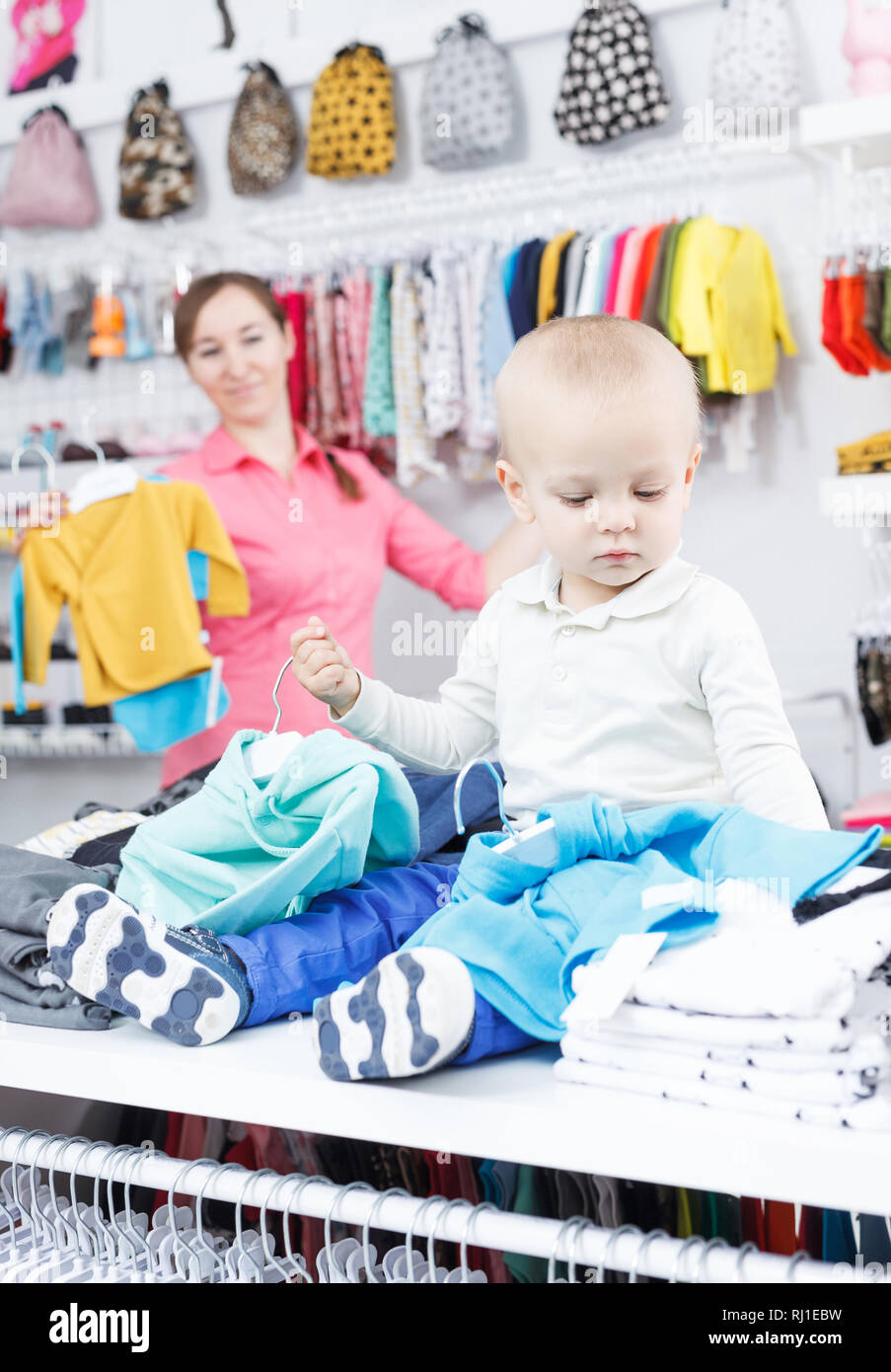 happy kid who is posing when his mother choosing clothes in the store ...