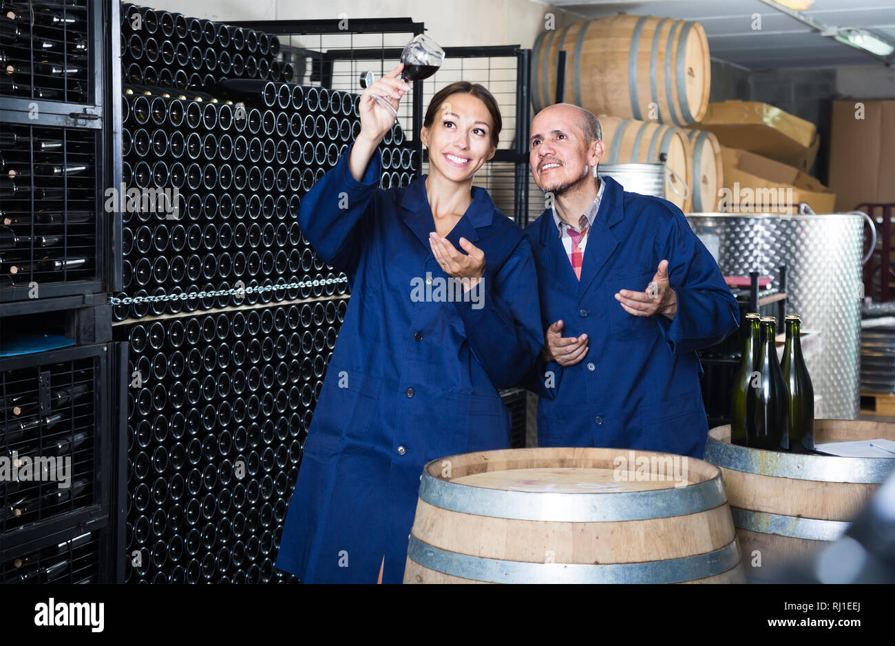 Two positive winery workers holding glass of wine in aging section of ...