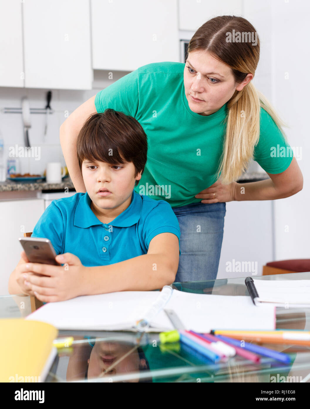 Tweenage boy sitting at kitchen using phone while mom scolding him ...