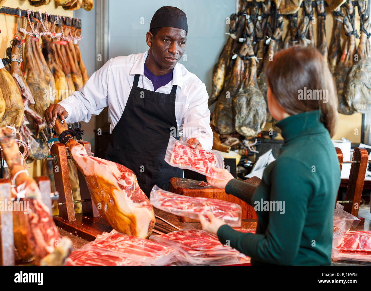 Positive African American salesman standing at counter in butcher shop ...