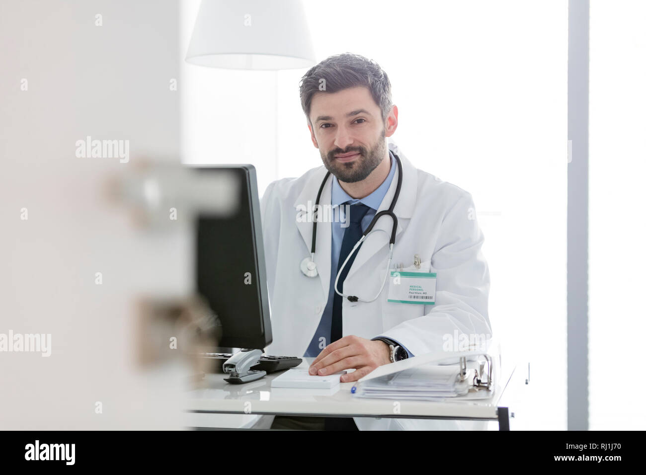 Portrait of confident doctor using computer at desk in hospital Stock ...