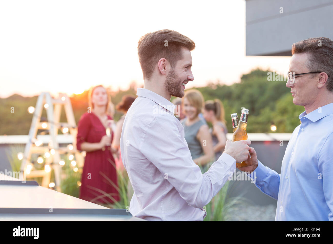 Businessmen toasting beer bottles during party on rooftop Stock Photo ...