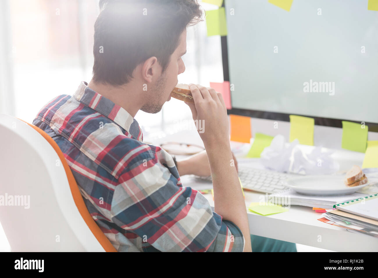 Businessman eating sandwich while sitting at computer desk Stock Photo ...