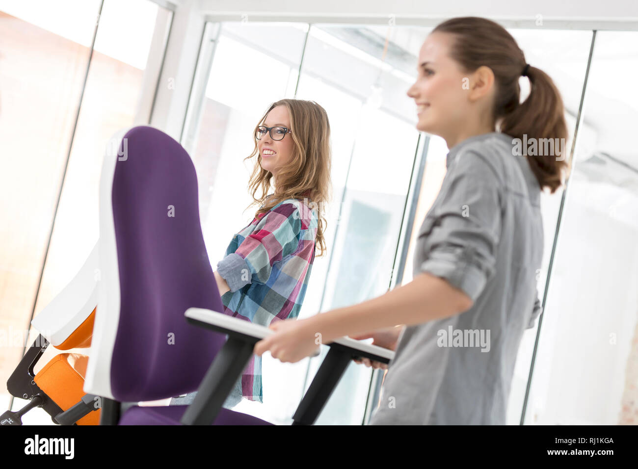 Smiling businesswomen carrying chairs in new office Stock Photo - Alamy
