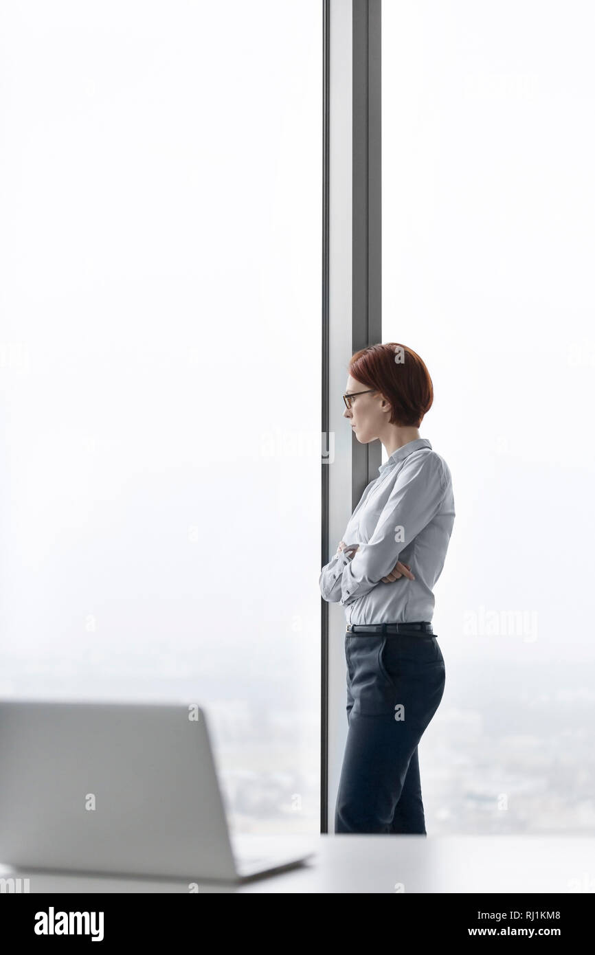 Side view of thoughtful young businesswoman looking through window at ... Side view of thoughtful young businesswoman looking through window at ...