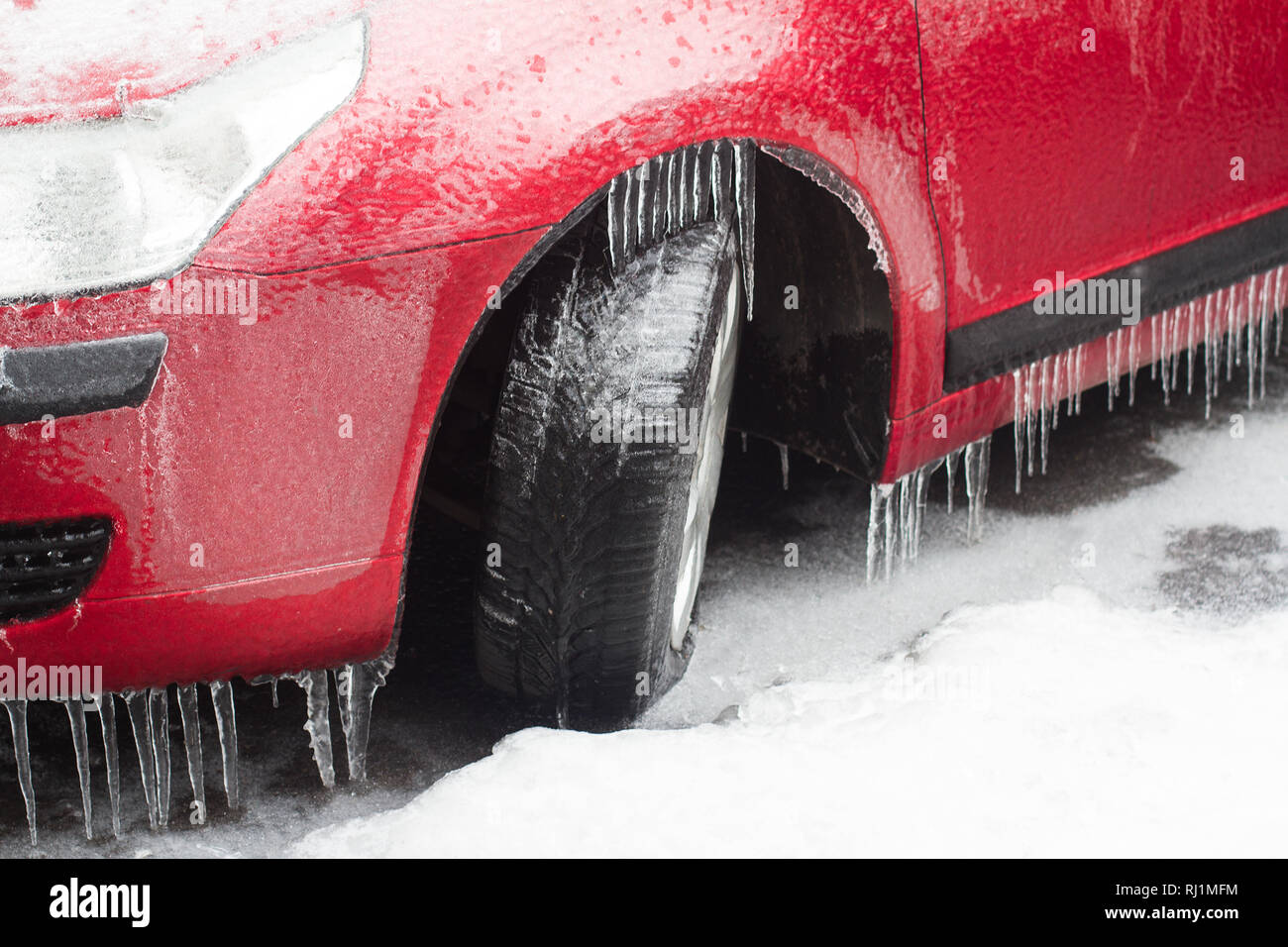 side view closeup of red frozen car with freezing rain icicles hanging ...
